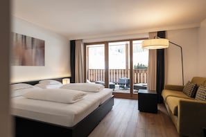 Quarto de hotel com cama, sofá, mesa pequena e varanda com vista para o exterior.