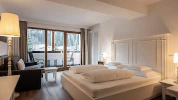 Quarto de hotel com uma cama grande, área de estar com uma cadeira e uma mesa, e varanda com vista para árvores.
