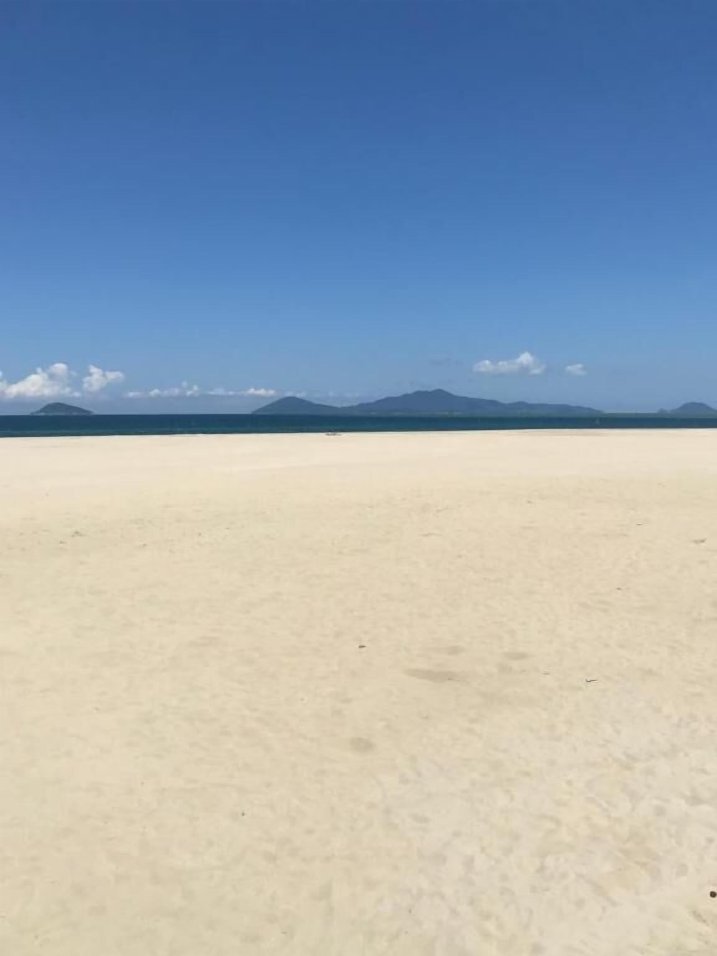Uma praia com céu claro e montanhas ao longe.