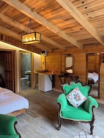 Interior de uma cabana de madeira com uma cama, uma poltrona verde, um banheiro e teto de madeira.