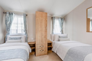 Quarto com duas camas, um guarda-roupa de madeira e uma janela com cortinas.