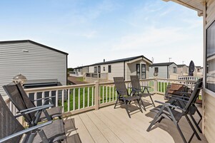 Um terraço com móveis de exterior, guarda-corpo branco e vista para casas móveis ao fundo.