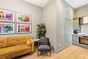 Uma sala de estar moderna com um sofá, poltrona e uma pequena mesa. Há quadros nas paredes e um vaso com planta.