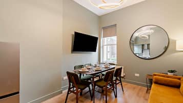 Uma sala de jantar com uma mesa posta para quatro pessoas, uma televisão na parede e um espelho grande.