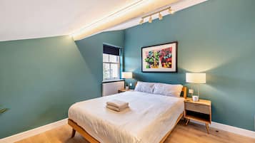 Quarto com cama, mesas de cabeceira, janela e uma obra de arte na parede.