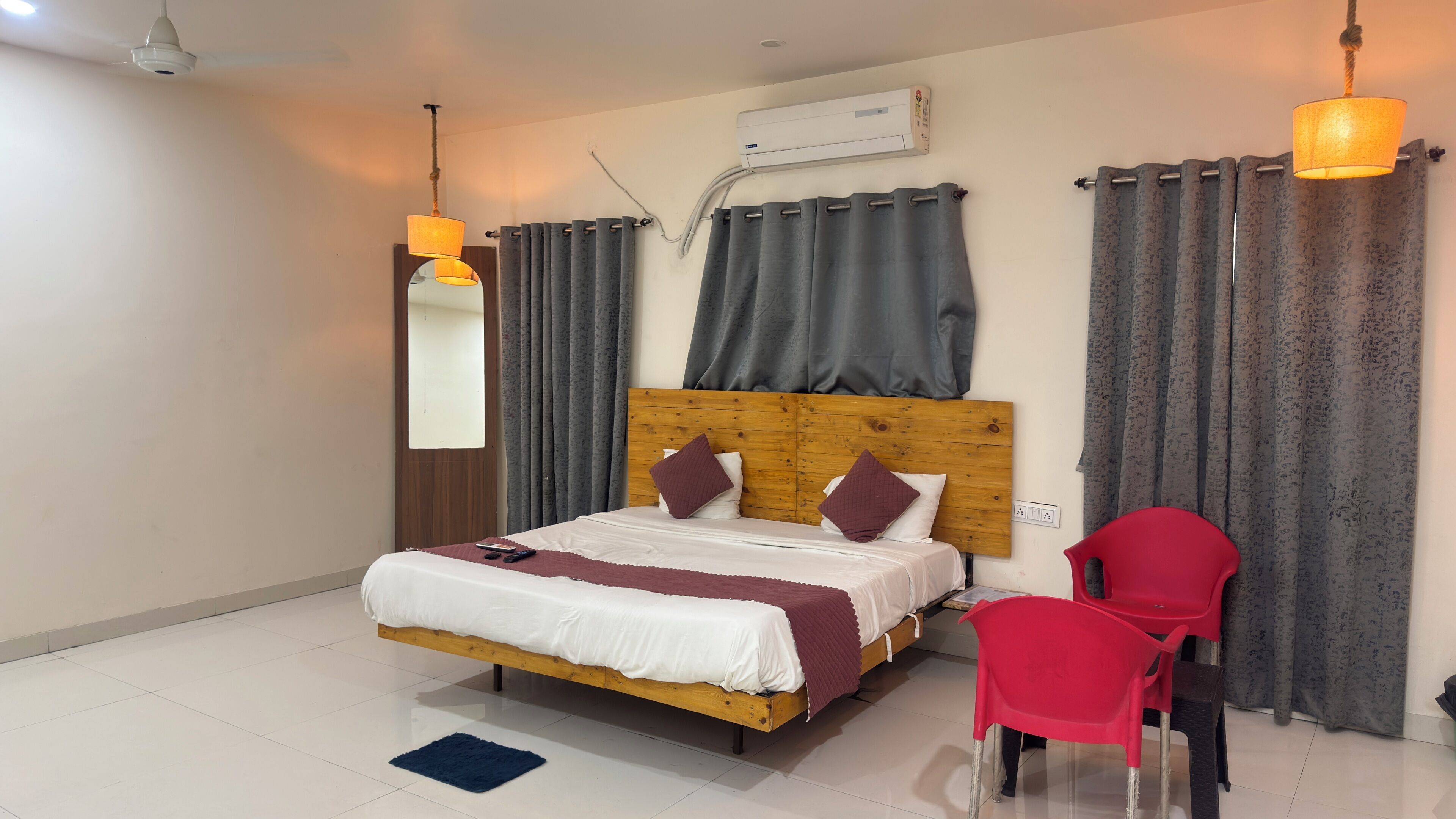 Um quarto com uma cama de madeira, cortinas cinzas, uma cadeira vermelha e um aparelho de ar condicionado na parede.
