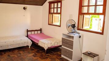 Quarto com duas camas de solteiro, piso de madeira, um ventilador e uma janela com persianas.