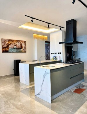 Uma cozinha moderna com uma ilha de mármore, fogão embutido e uma luminária pendente.