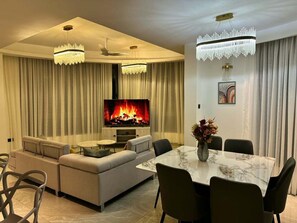 Uma sala de estar moderna com lareira, área de jantar e uma televisão grande.