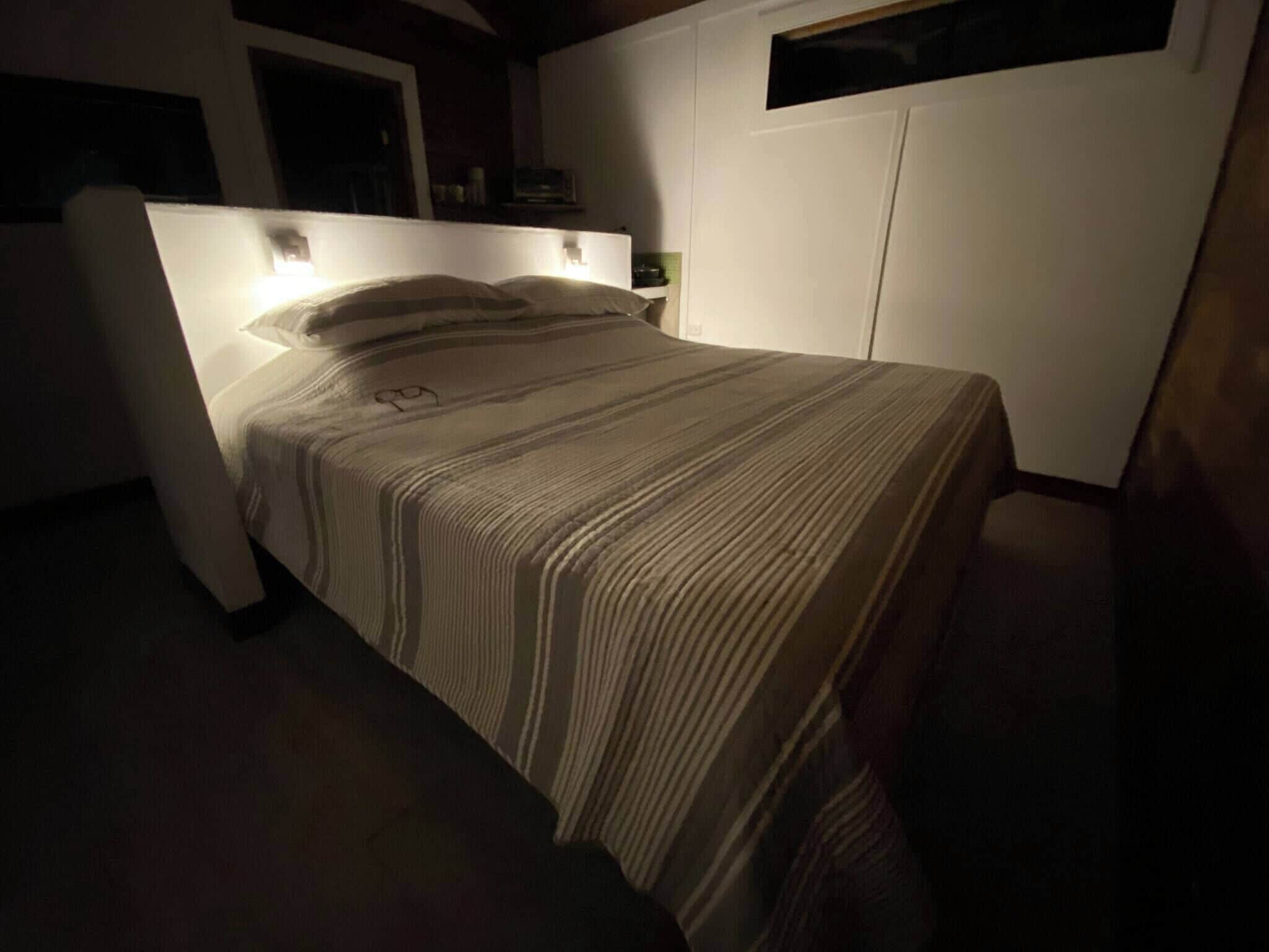 Cama com colcha listrada num quarto com pouca luz.