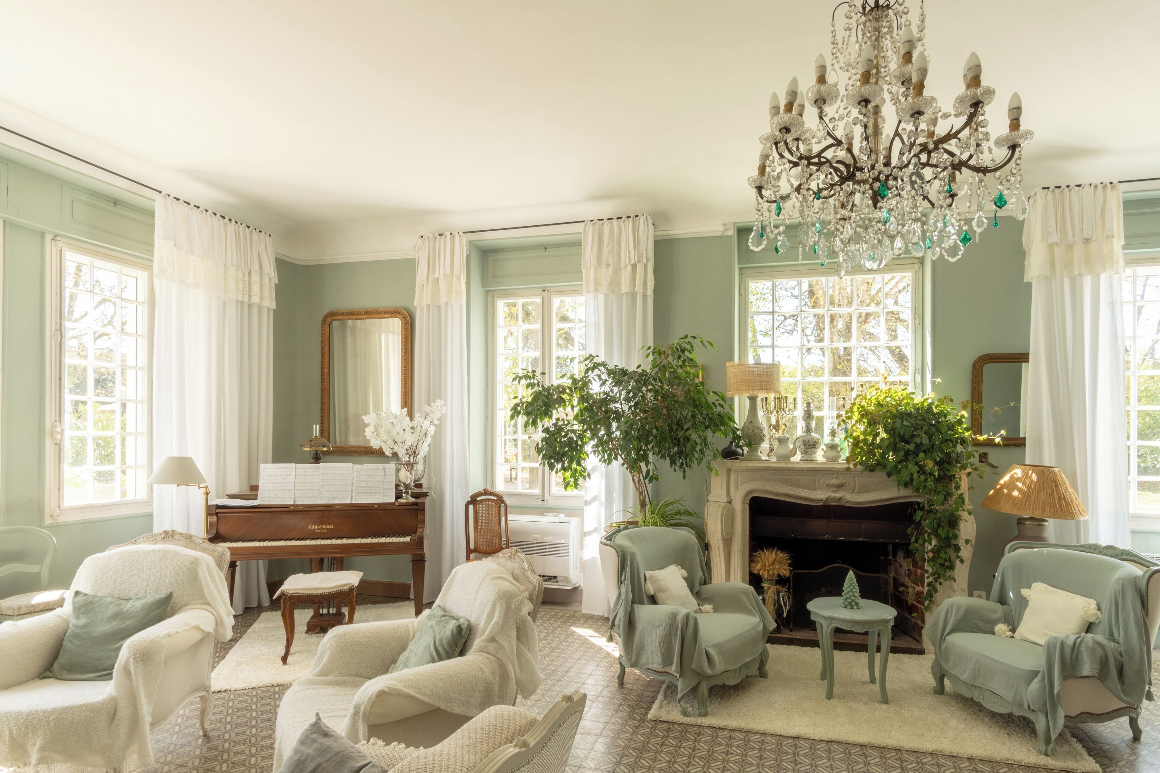 Um quarto com piano, duas poltronas, lareira e um candelabro.