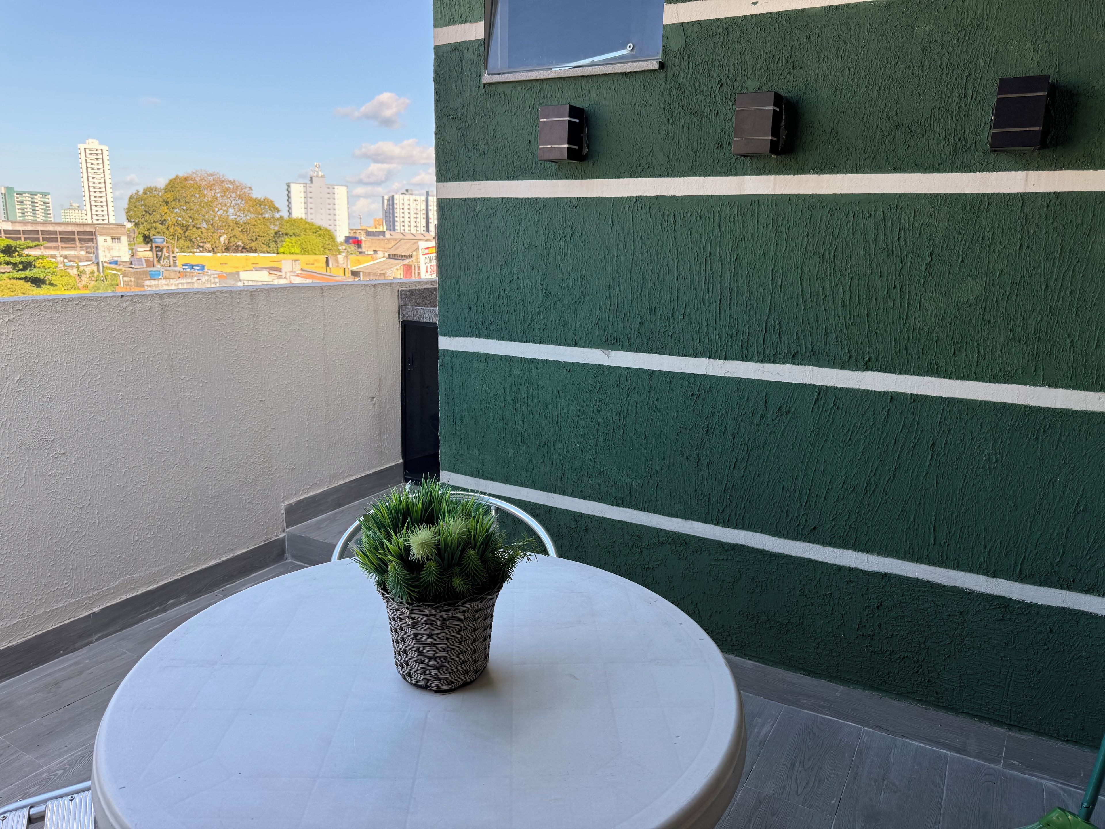 Mesa redonda com planta em vaso numa varanda com parede verde e janela.