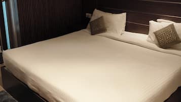 Uma cama grande com cabeceira escura, roupa de cama branca e almofadas estampadas.