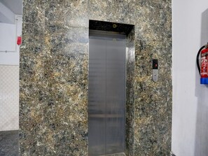Um elevador com interior metálico, instalado num espaço com parede de granito salpicado.