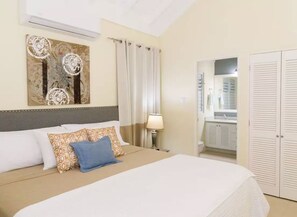 Quarto de hotel com cama, mesa de cabeceira, luminária, banheiro com espelho e guarda-roupa.