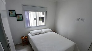 Quarto com cama, mesa de cabeceira, janela e dois interruptores de luz na parede.