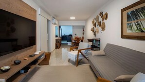Uma sala de estar moderna com televisão de tela plana, sofá, área de refeições e uma parede decorada com chapéus.