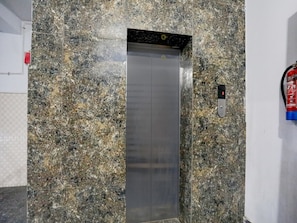 Um elevador com interior metálico e parede de granito ao redor.