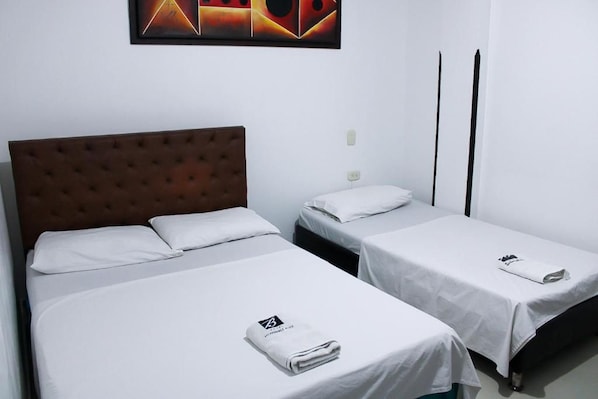 Quarto de hotel com duas camas de solteiro, cabeceira marrom, roupa de cama branca e um quadro abstrato emoldurado na parede.