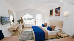 Quarto de hotel com cama, mesa de cabeceira, televisão e vista através de uma janela em arco.