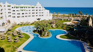 Um resort com uma piscina grande, uma praia e um edifício branco com várias varandas.