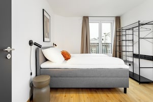 Um quarto moderno com um sofá-cama cinzento, uma luminária de cabeceira, um quadro emoldurado e um varal de metal.