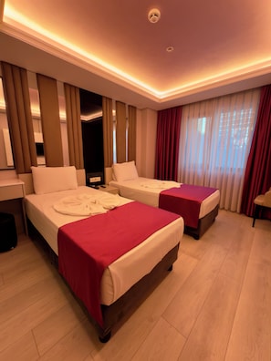 Quarto de hotel com duas camas, uma escrivaninha e uma cadeira.