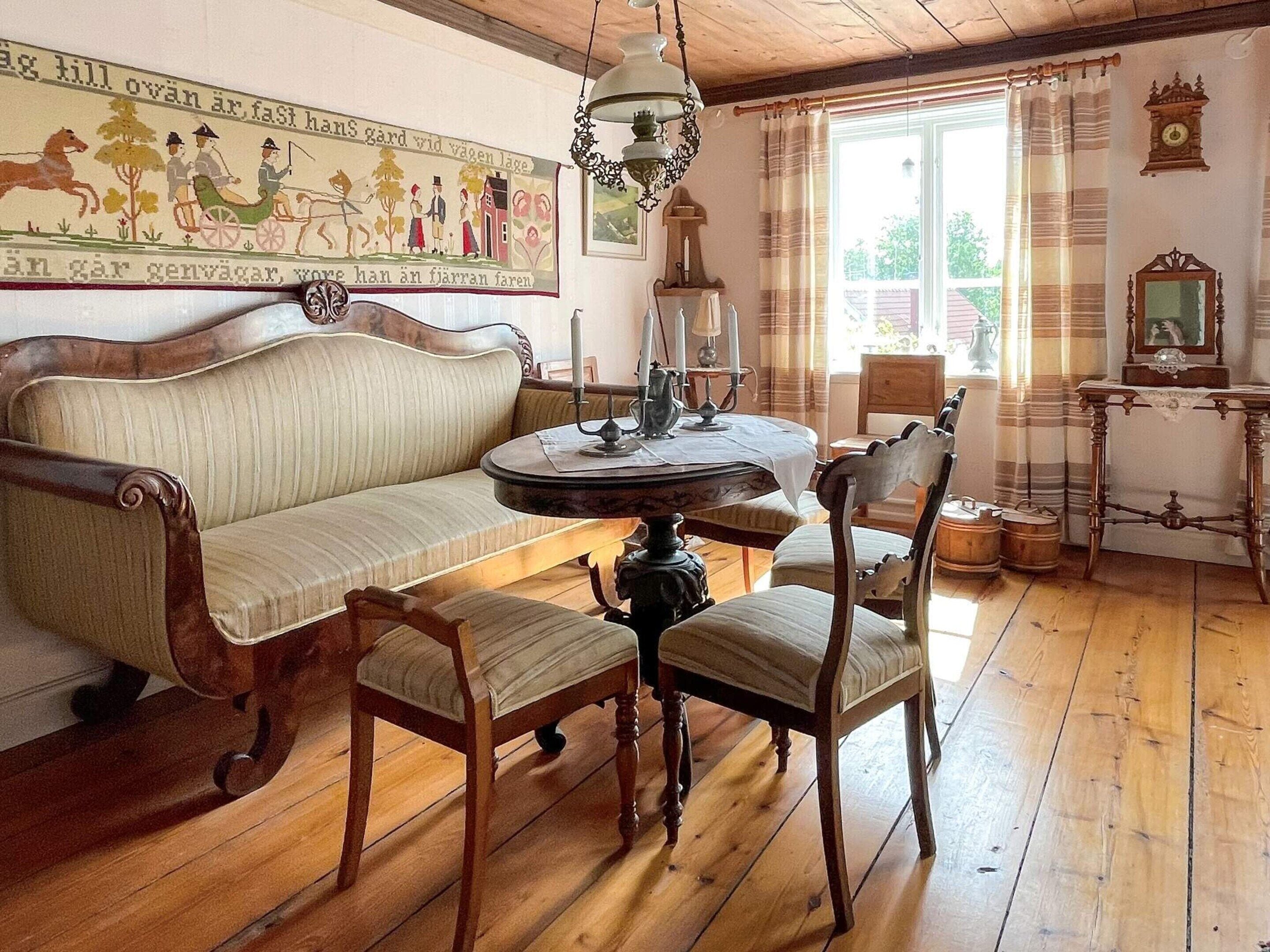 Quarto tradicional com piso de madeira, uma mesa redonda com velas, um sofá e uma cadeira.