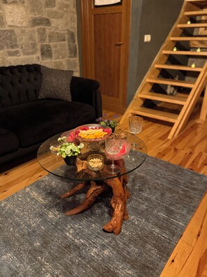 Uma mesa de centro com tampo de vidro e base de madeira, rodeada por objetos decorativos e uma tigela de vidro.