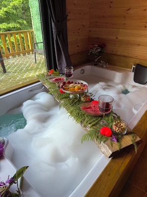 Uma cabana de madeira com uma banheira cheia de espuma, rodeada por diversas frutas, nozes e uma taça de vinho tinto.
