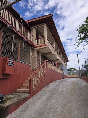 Um edifício de vários andares com fachada vermelha, uma escadaria que leva ao andar superior e uma entrada gradeada.