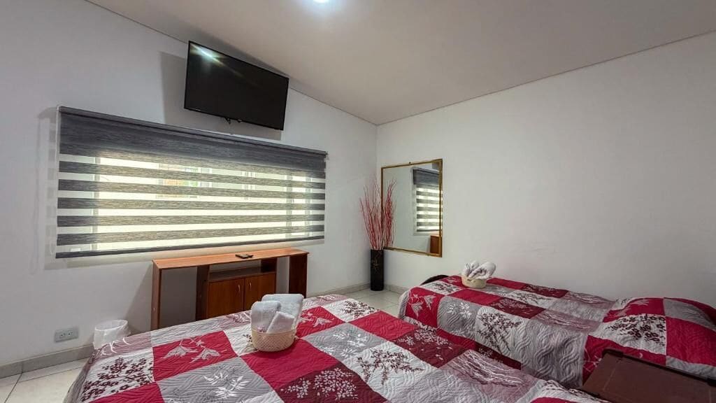Quarto com duas camas, televisão, espelho e janela com persianas.