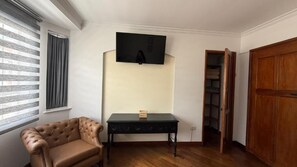 Quarto com sofá de couro, armário de madeira, televisão na parede e porta de madeira.