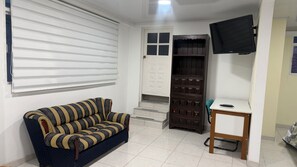 Quarto com sofá, televisão, porta e uma pequena mesa.