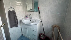 Uma casa de banho com uma pia branca, um espelho, um porta-toalhas e um esfregão.