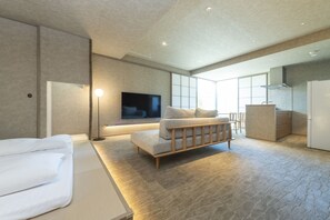 Quarto de hotel moderno com televisão de tela plana, sofá, cama, escrivaninha e cozinha.