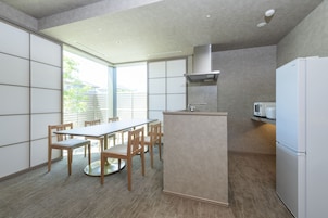 Uma cozinha moderna com área de refeições, apresentando uma ilha central, cadeiras de madeira e uma geladeira branca.