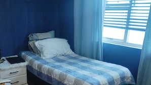 Um quarto com uma cama, cômoda, cadeira e janela com cortinas.
