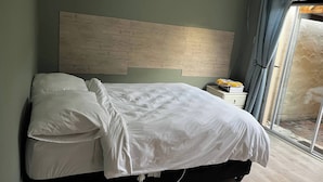 Quarto com cama, mesa de cabeceira e janela com cortinas.