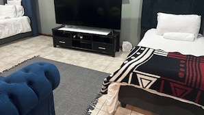 Quarto de hotel com cama, sofá, televisão e uma pequena mesa.