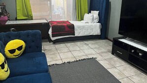 Quarto com cama, sofá com almofada, televisão e janela com cortinas.