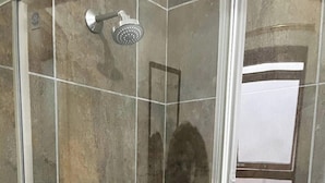 Chuveiro com porta de vidro, paredes revestidas de azulejos e um detalhe em mosaico no canto.