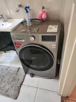 Máquina de lavar e secar compacta com painel de controle, um borrifador de aromatizante e uma esponja de banho rosa.