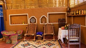 Quarto tradicional com duas escadas de madeira, cadeiras de vime, tapete estampado e uma mesa com toalha branca.