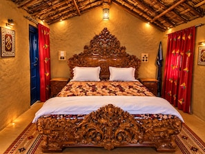 Quarto tradicional com cabeceira de madeira entalhada, colcha estampada e cortinas vermelhas com desenhos geométricos.