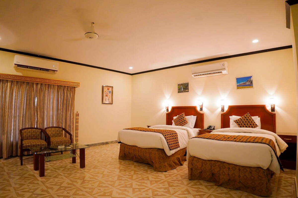 Quarto de hotel com duas camas, uma cadeira, um ar condicionado e piso estampado.