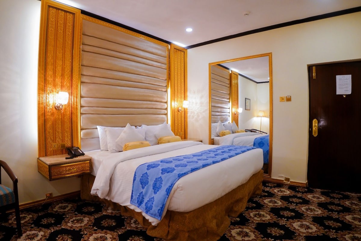 Quarto de hotel com uma cama grande, mesas de cabeceira, escrivaninha e guarda-roupa.