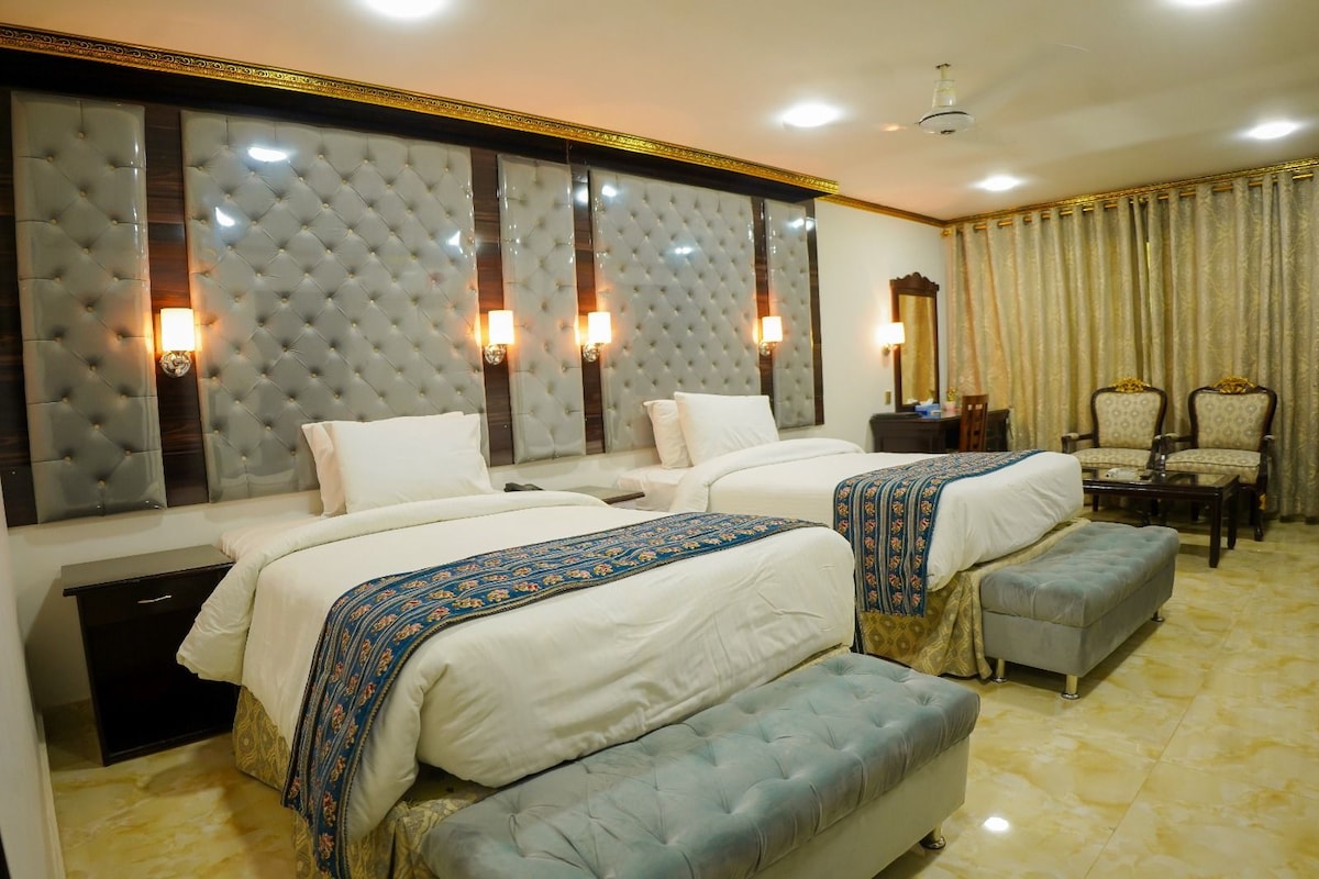 Quarto de hotel com duas camas, um espaço para sentar e um espelho grande.