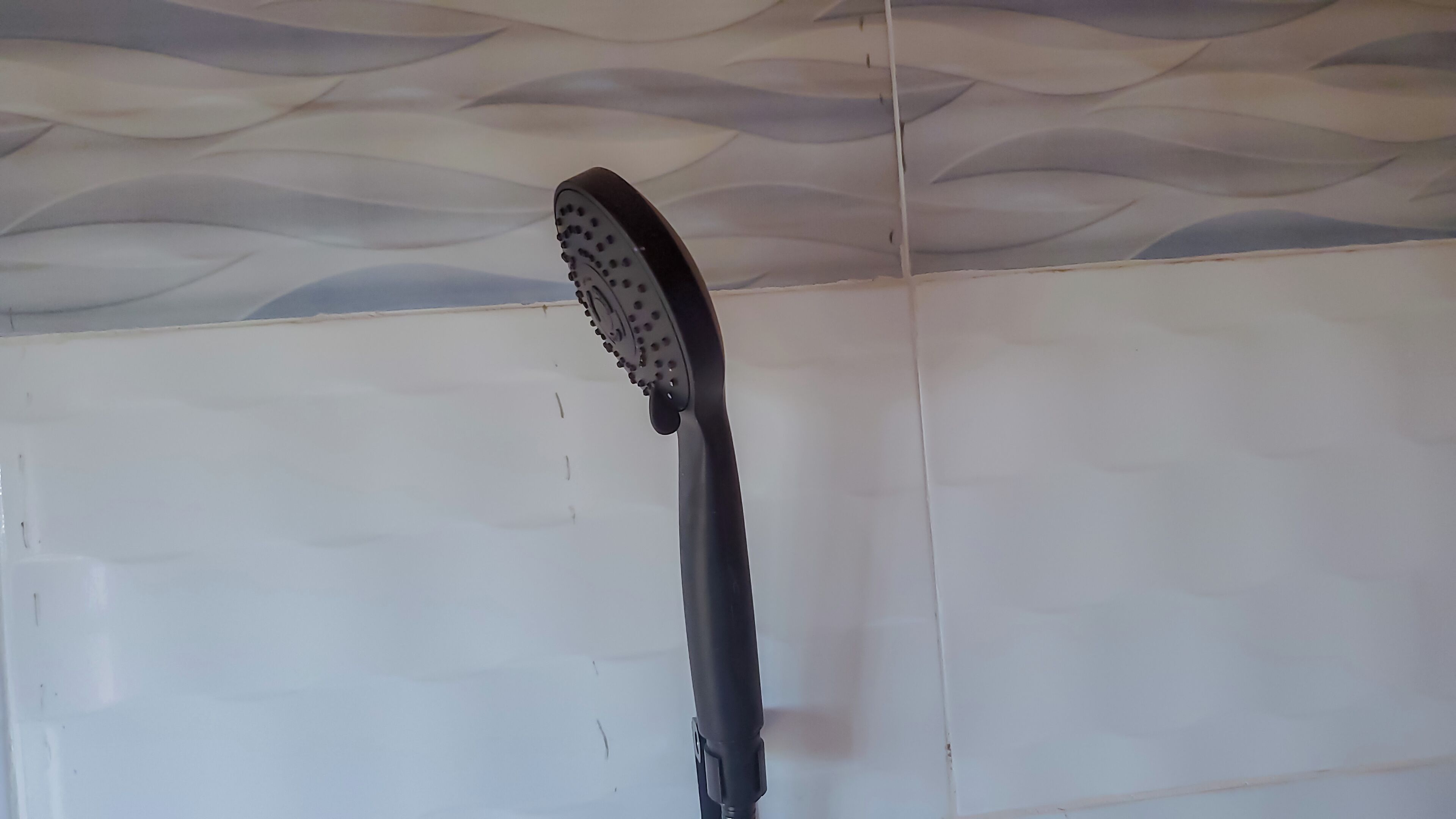 Chuveiro preto fixado em parede branca com teto texturizado.