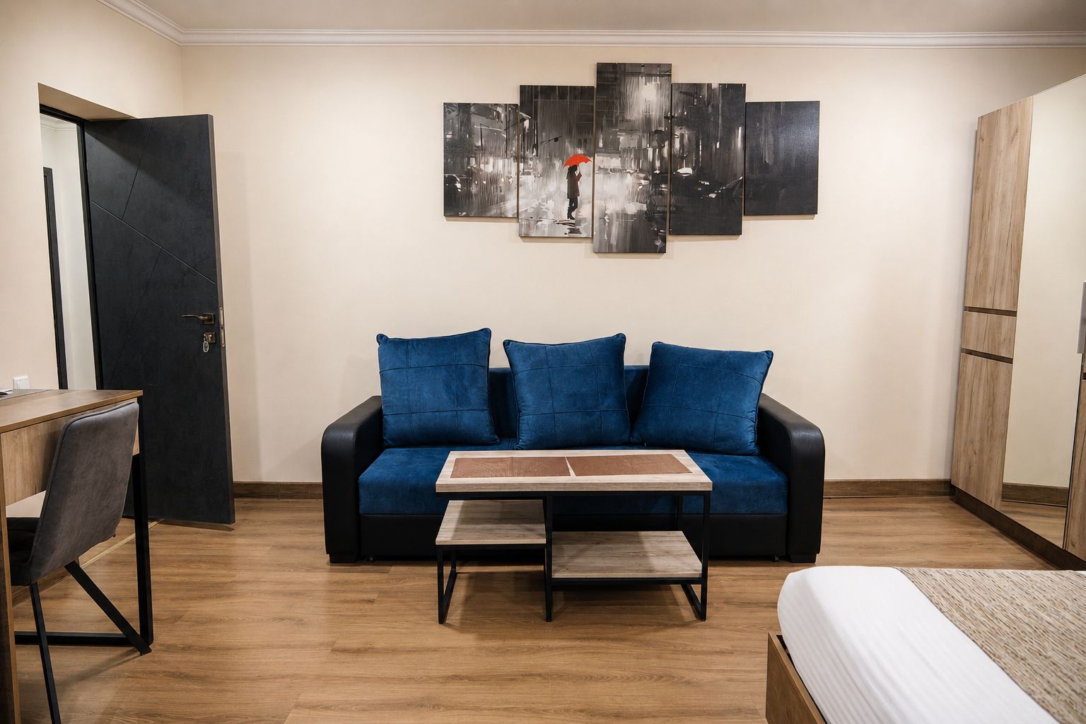 Quarto moderno com sofá preto, mesa de centro de madeira, cama e uma obra de arte na parede.